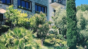 Uma pessoa sentada perto de uma piscina, com vista para um edifício de pedra e vegetação exuberante.