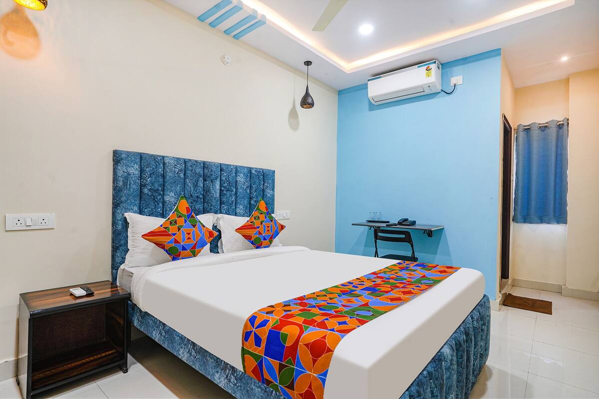 Quarto de hotel bem arrumado, com uma cama grande, uma mesa de cabeceira, uma escrivaninha e um aparelho de ar condicionado.