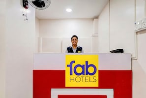 Bancada de recepção de hotel com um letreiro 'fab hotels', um telefone e um ventilador fixado na parede.