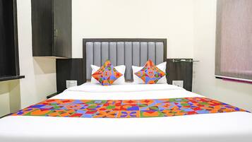 Uma cama com colcha de padrão geométrico colorido, duas almofadas com desenho semelhante, um painel de cabeceira estofado cinza e um guarda-roupa de madeira escura.