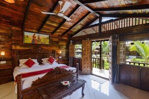 Quarto de madeira com uma cama, um ventilador de teto e vista para o verde lá fora.