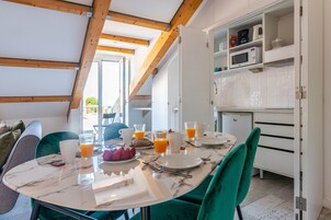 Cenário de café da manhã com mesa posta para dois, micro-ondas e armário com utensílios de cozinha.
