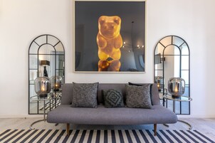 Uma sala de estar moderna com um sofá cinzento, duas mesas laterais com tampos de vidro e uma grande obra de arte em formato de urso sobre o sofá.