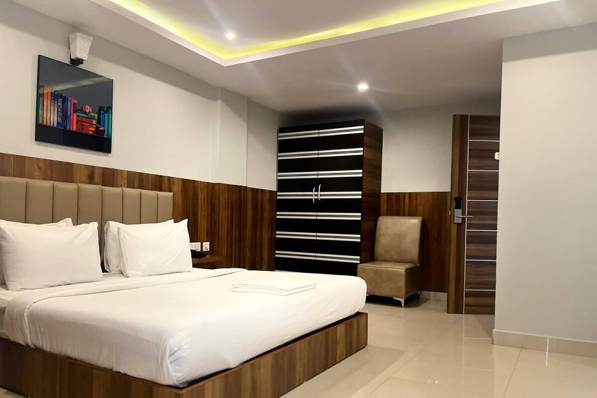 Quarto moderno com uma cama grande, cabeceira de madeira, estante e uma cadeira.