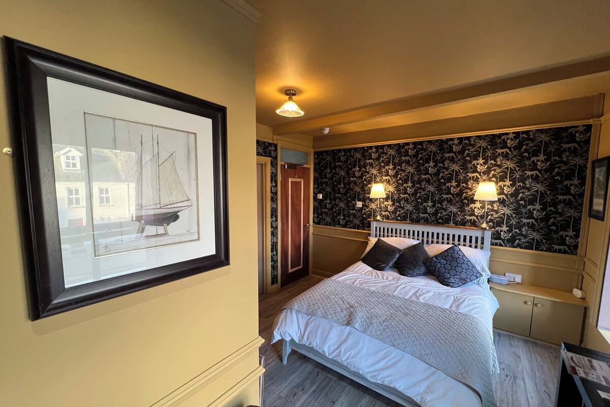 Quarto com cama, quadro na parede, porta e parede com padrão floral.