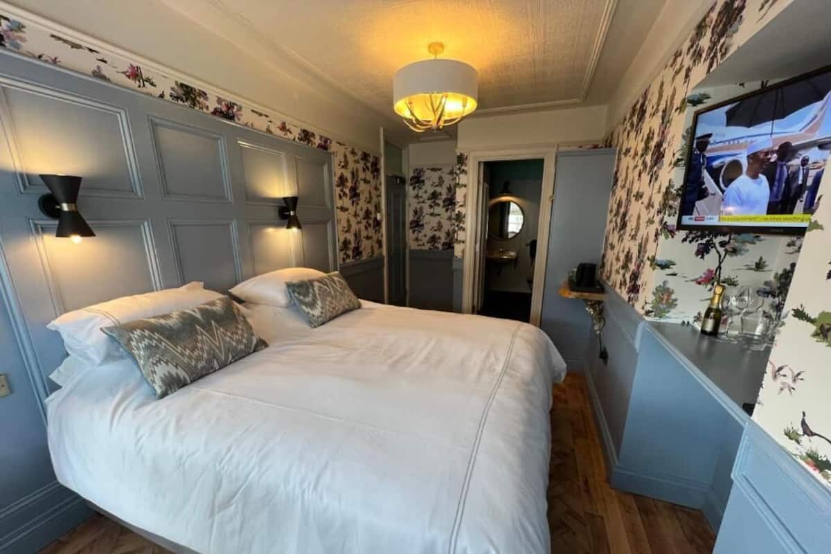 Quarto com uma cama grande, duas luminárias de cabeceira, televisão na parede e papel de parede floral.