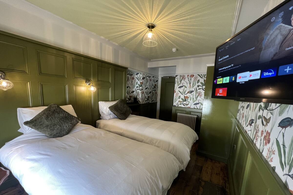 Quarto de hotel com duas camas, televisão na parede e papel de parede com padrão floral.