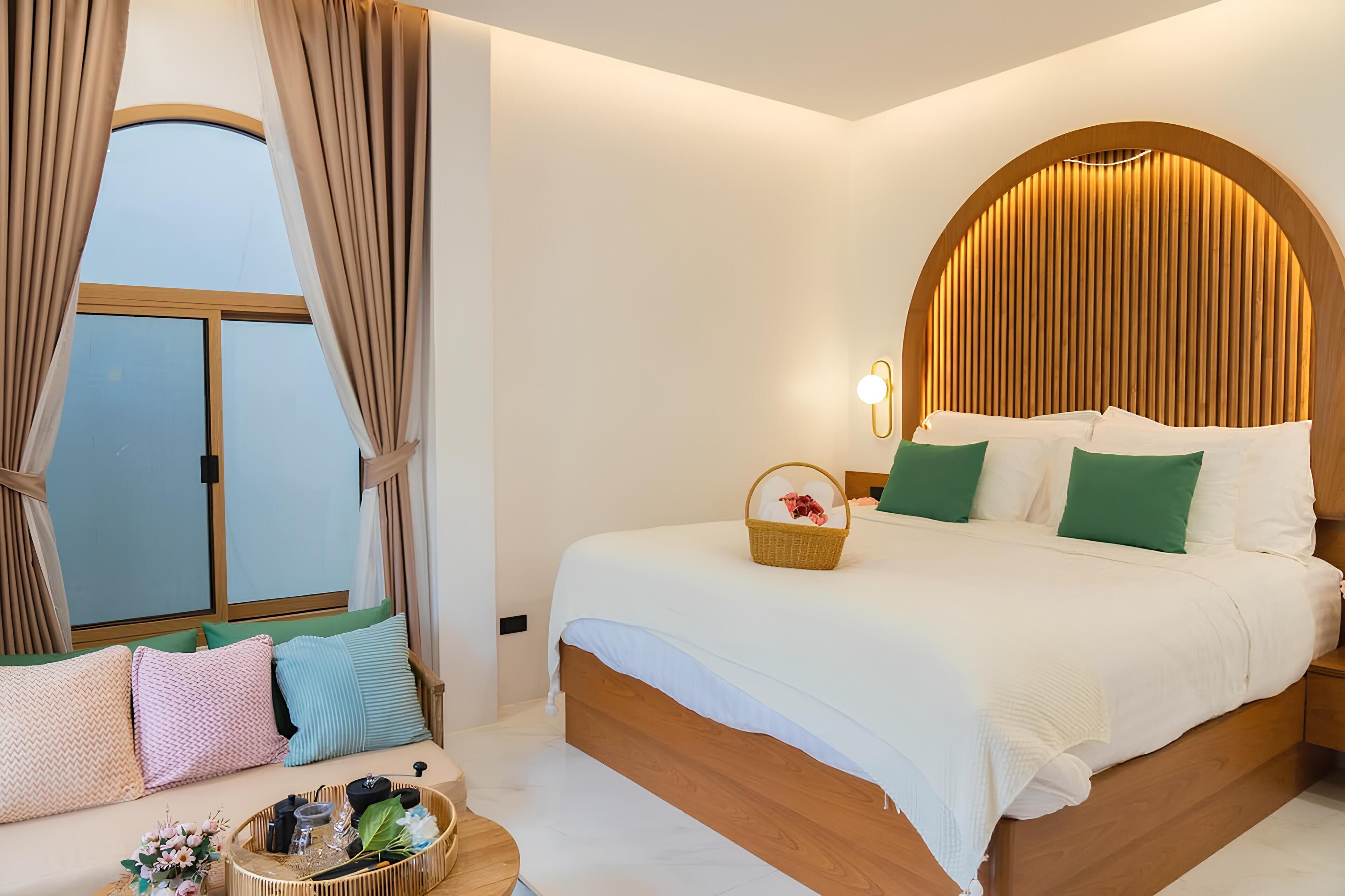 Quarto com cama grande, cabeceira de madeira, janela com cortinas e mesa de cabeceira com cesto.