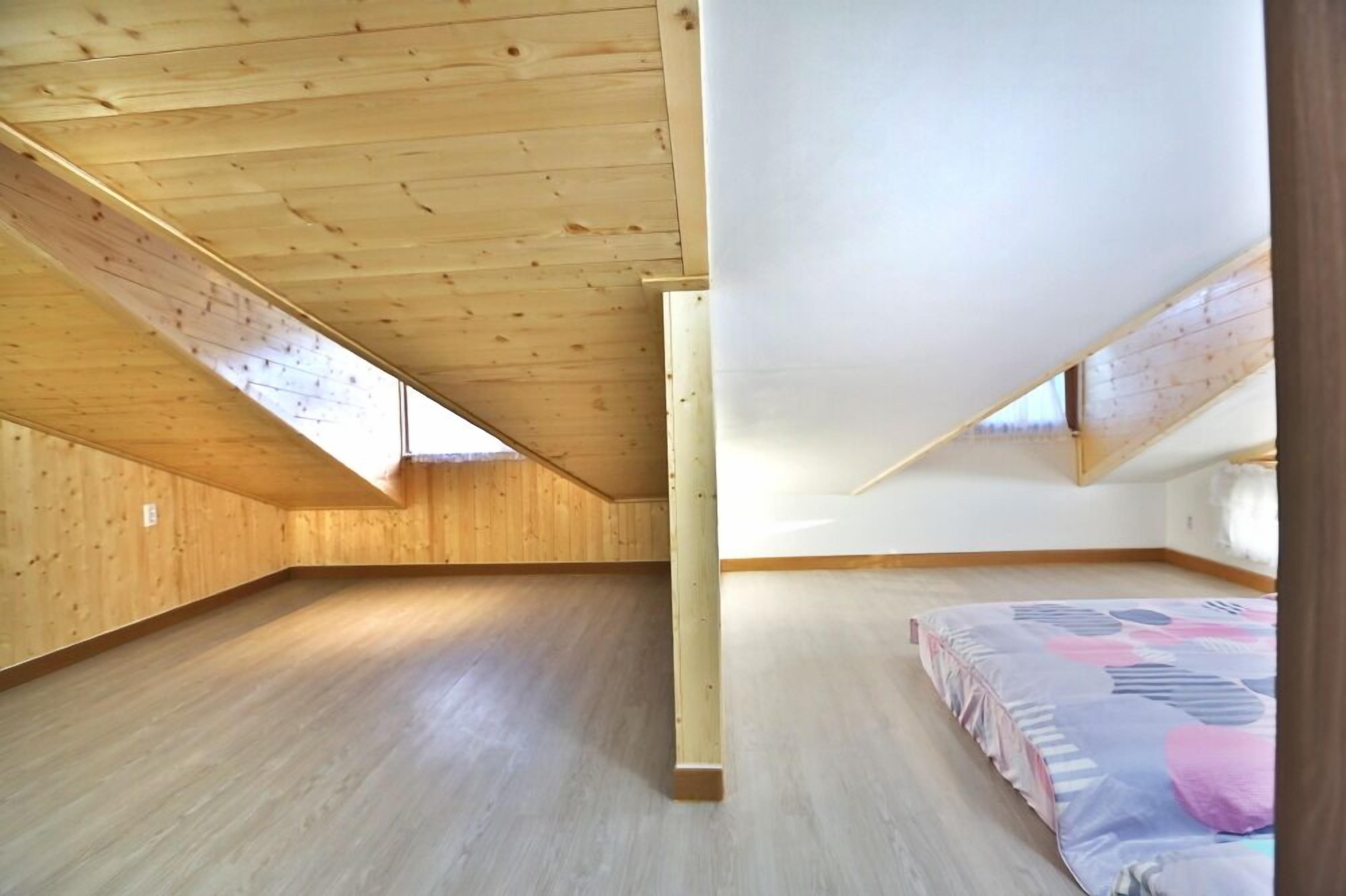 Um quarto com teto inclinado, paredes de madeira e cama com manta colorida.