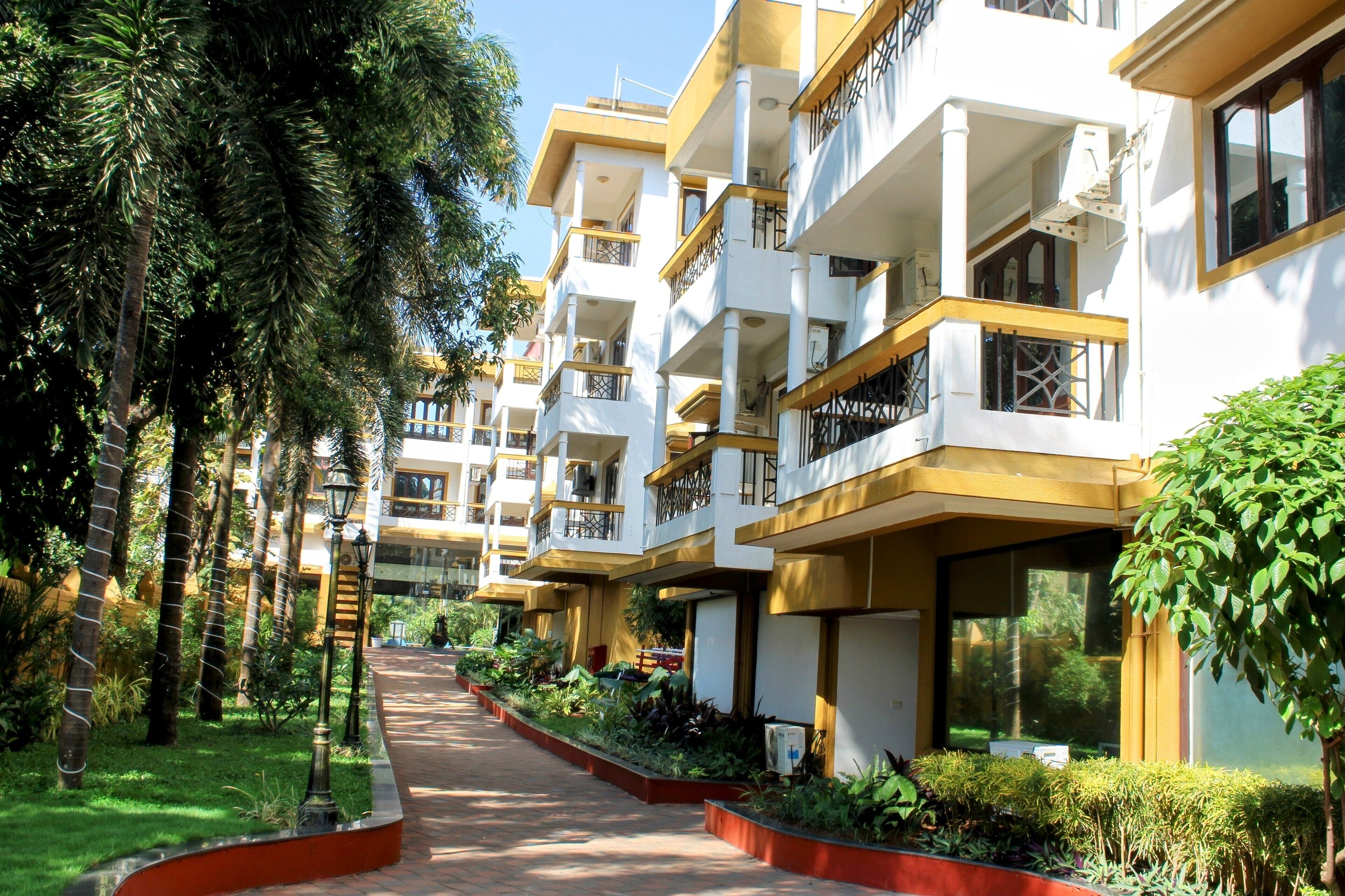 Um hotel com vários andares, varandas, um caminho central e vegetação exuberante.