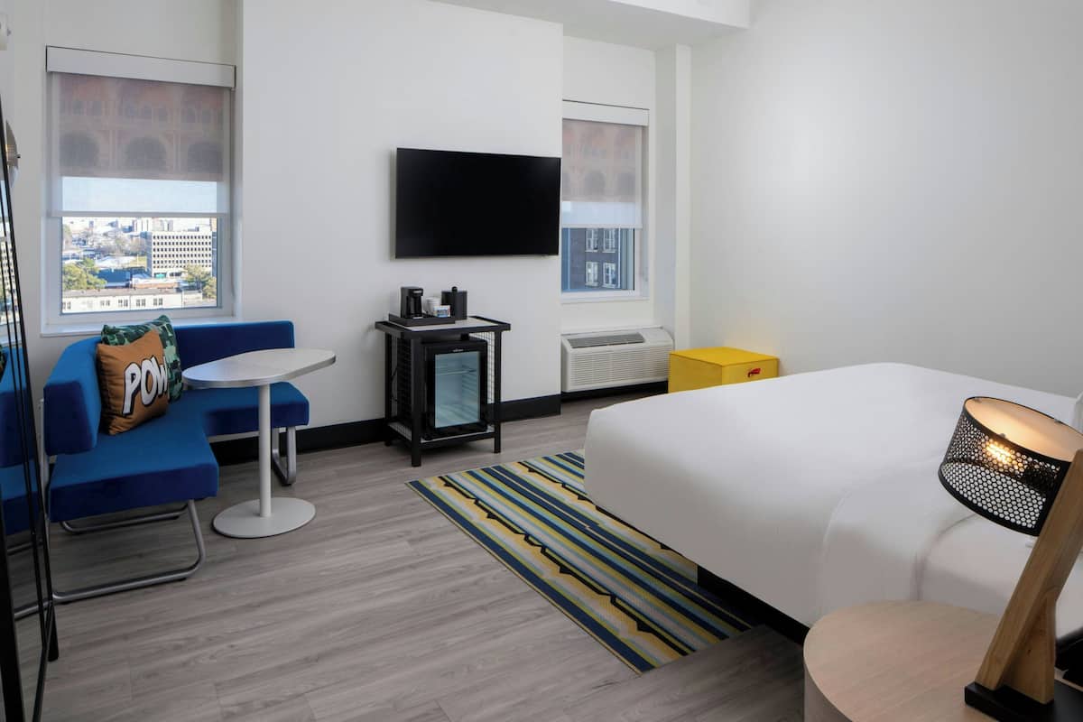 Quarto de hotel moderno com cama, escrivaninha, cadeira, televisão e janela com vista para a cidade.