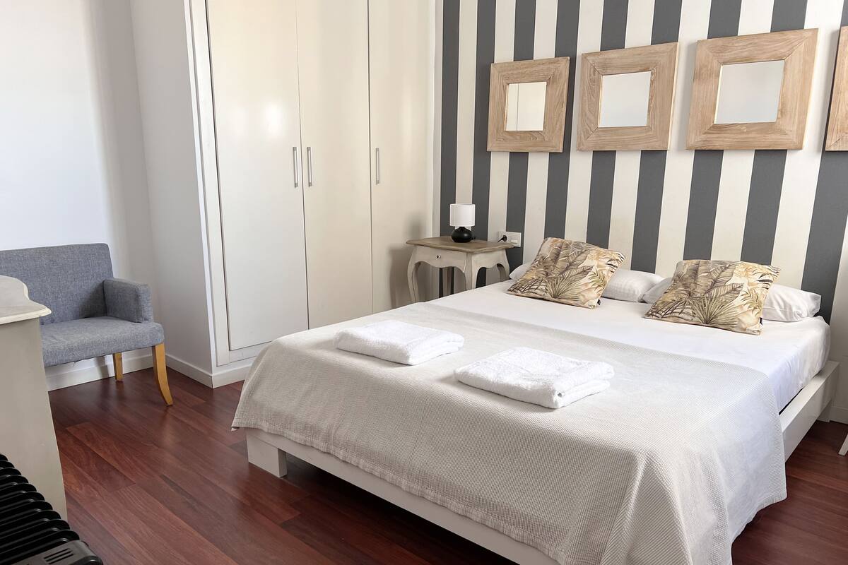 Quarto bem arrumado com cama, almofadas e mesa de cabeceira.