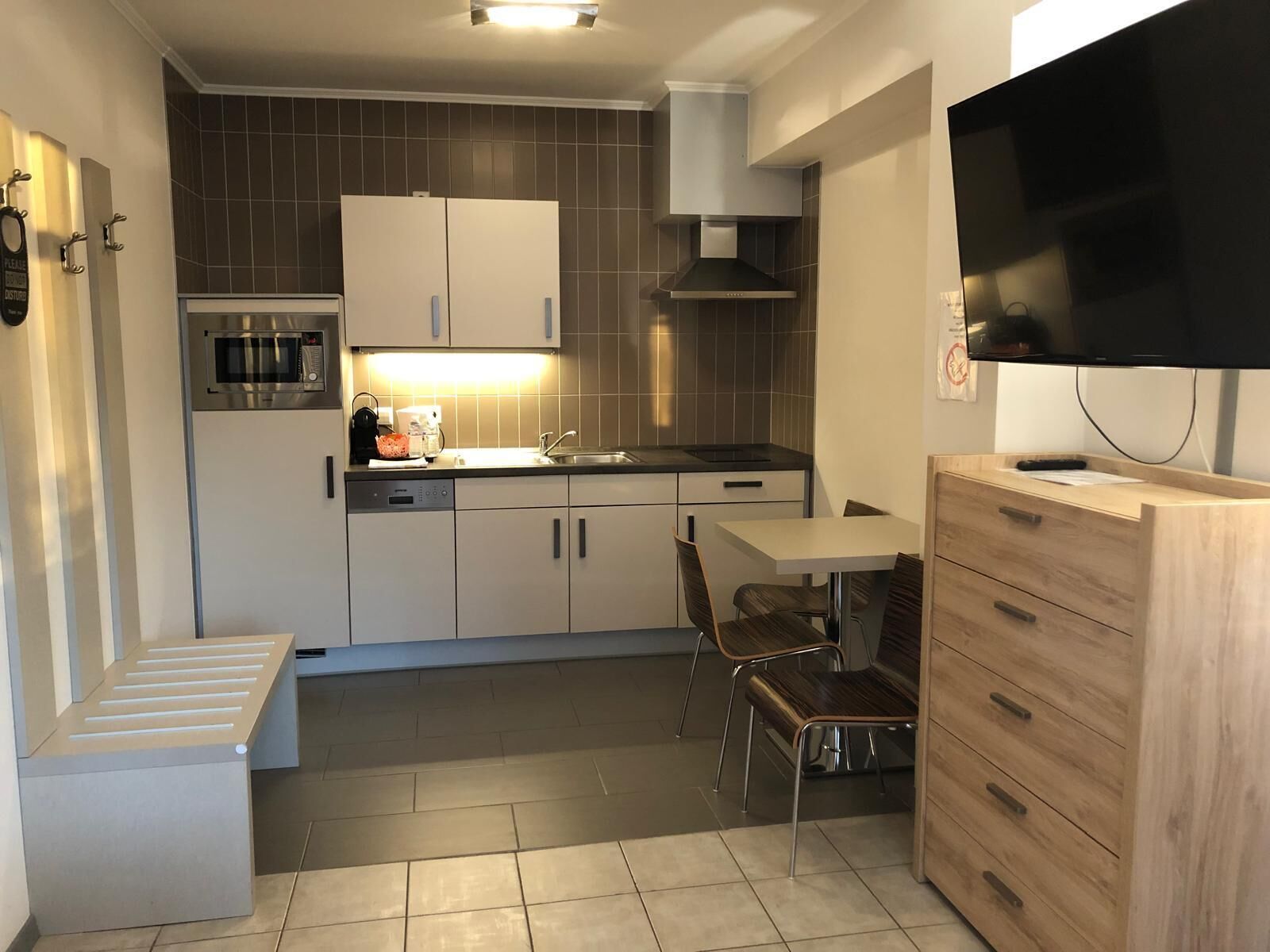 Uma cozinha compacta com armários brancos, micro-ondas, pia e área de refeições com mesa e cadeiras.