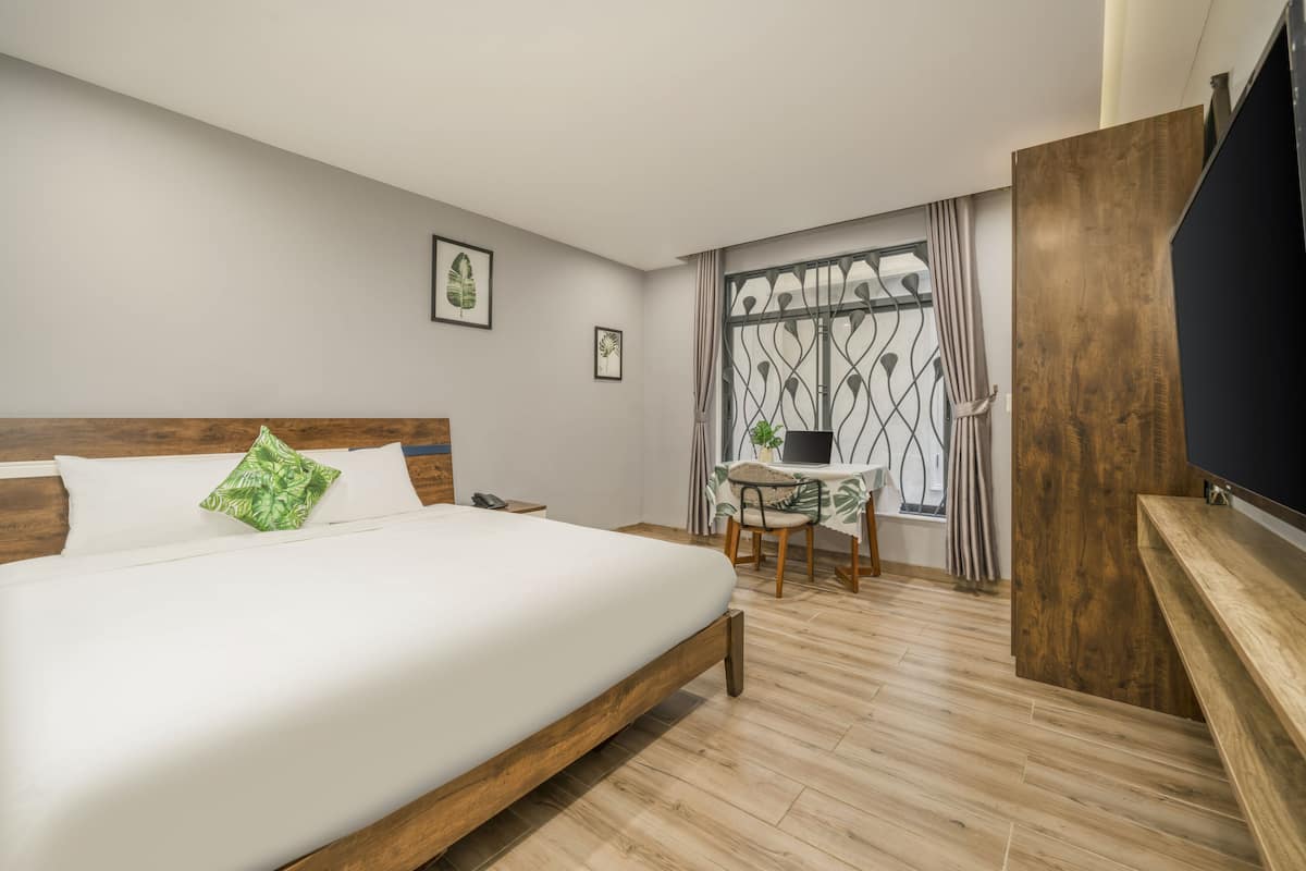 Quarto de hotel com cama, escrivaninha, cadeira, televisão e janela com cortinas.
