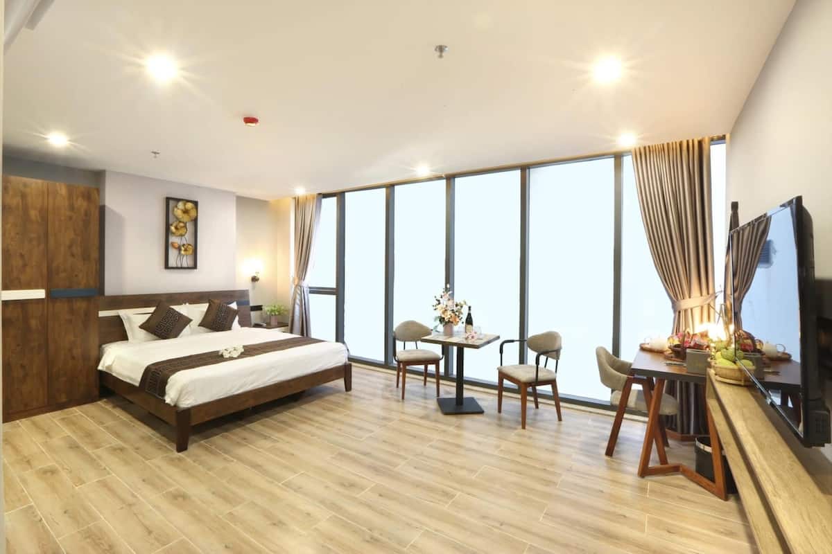 Quarto de hotel moderno com uma cama grande, área de refeições e televisão.