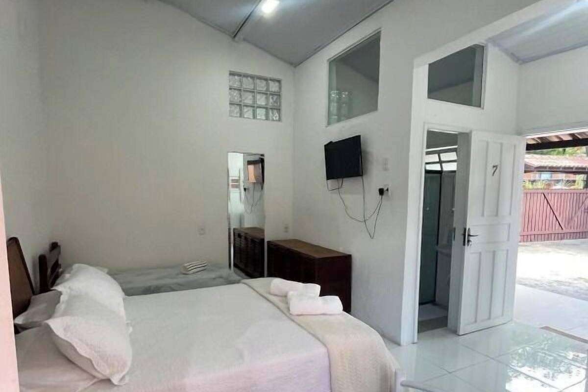 Quarto com duas camas, TV fixada na parede e porta que dá para o exterior.