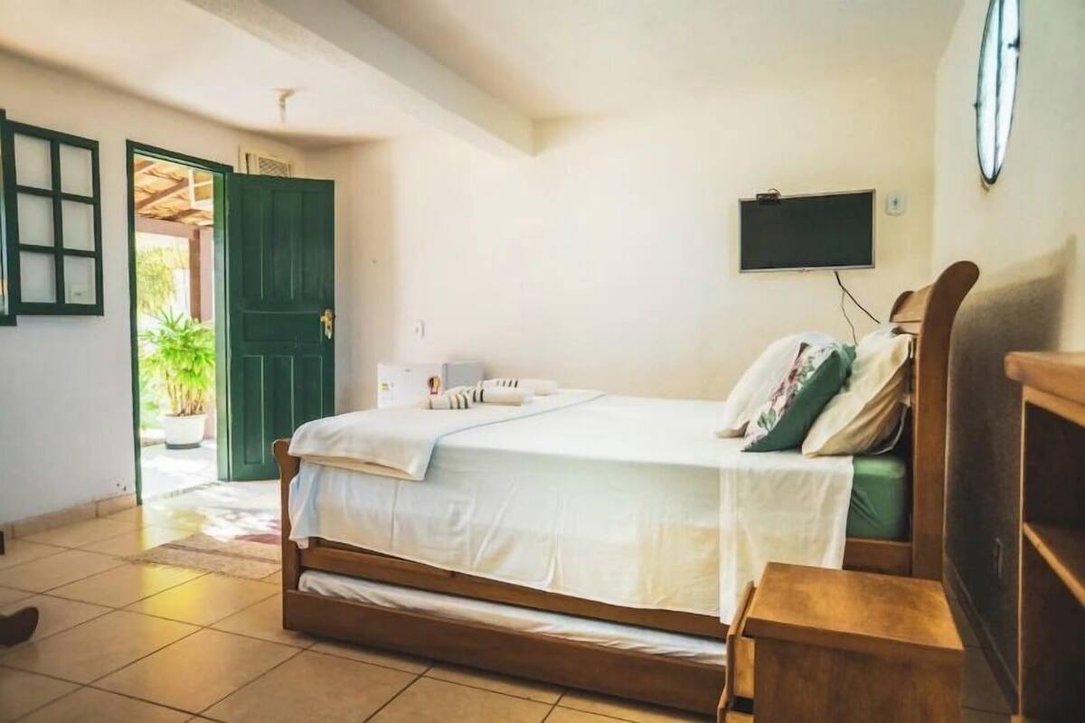 Quarto com cama, televisão na parede e porta que dá para o exterior.