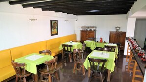 Uma sala de jantar com mesas e cadeiras de madeira, toalhas de mesa verdes e uma parede amarela.