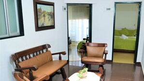 Quarto com sofá de madeira, uma cadeira de madeira e uma pequena mesa com uma planta.
