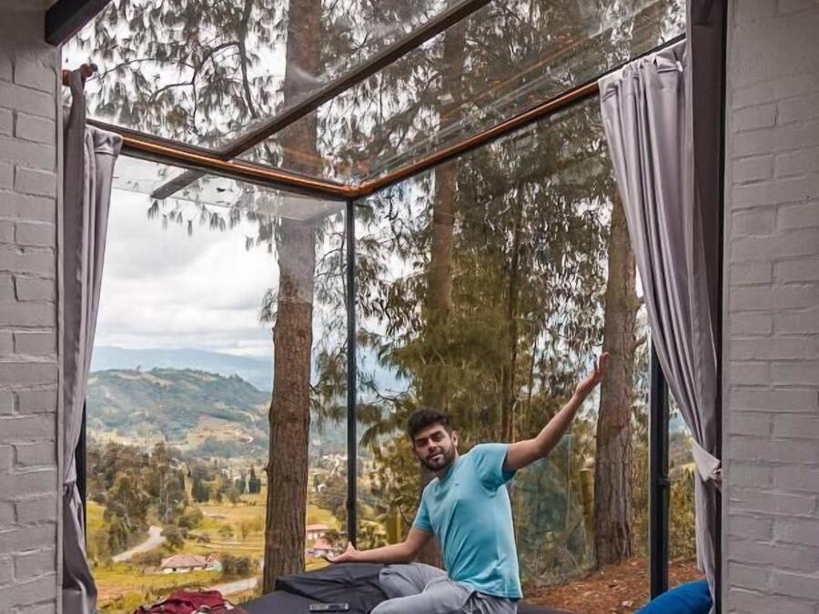 Quarto com uma grande janela que oferece vista para árvores e colinas.