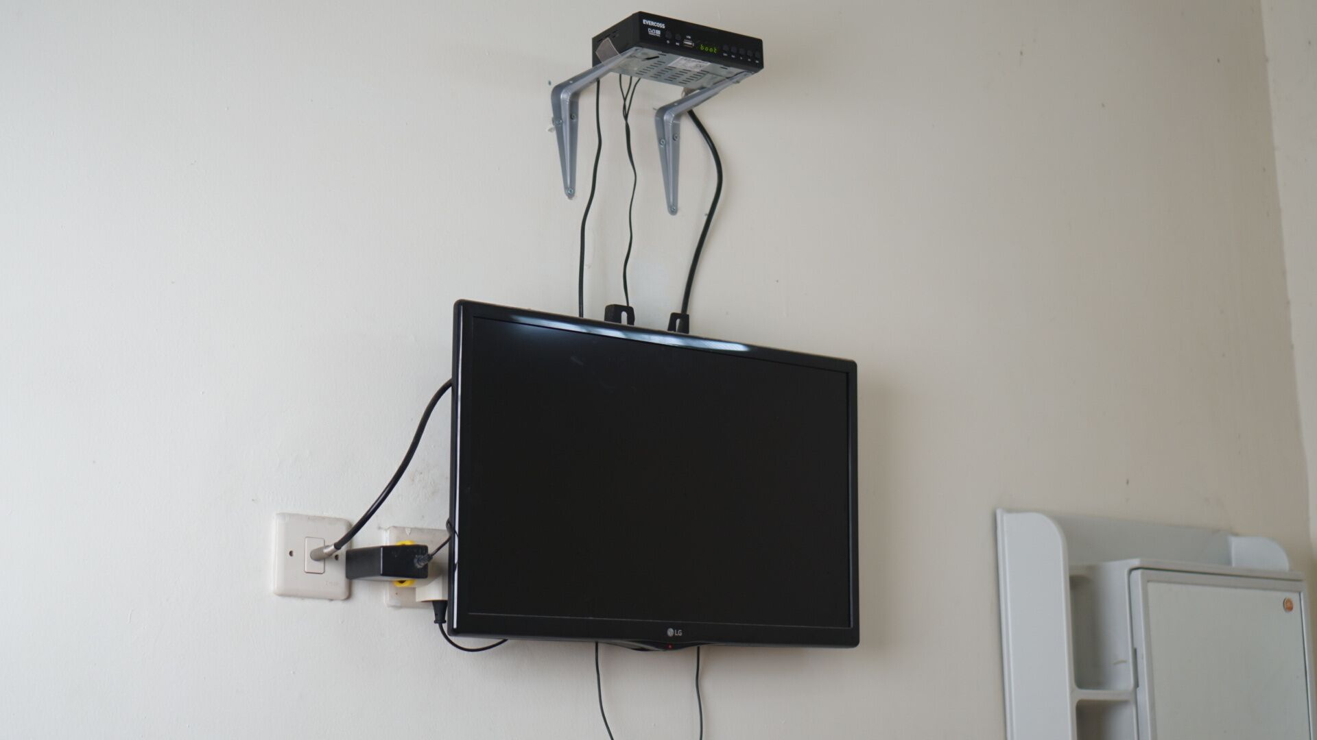 Televisão de tela plana fixada na parede, com um filtro de tomada e cabos.