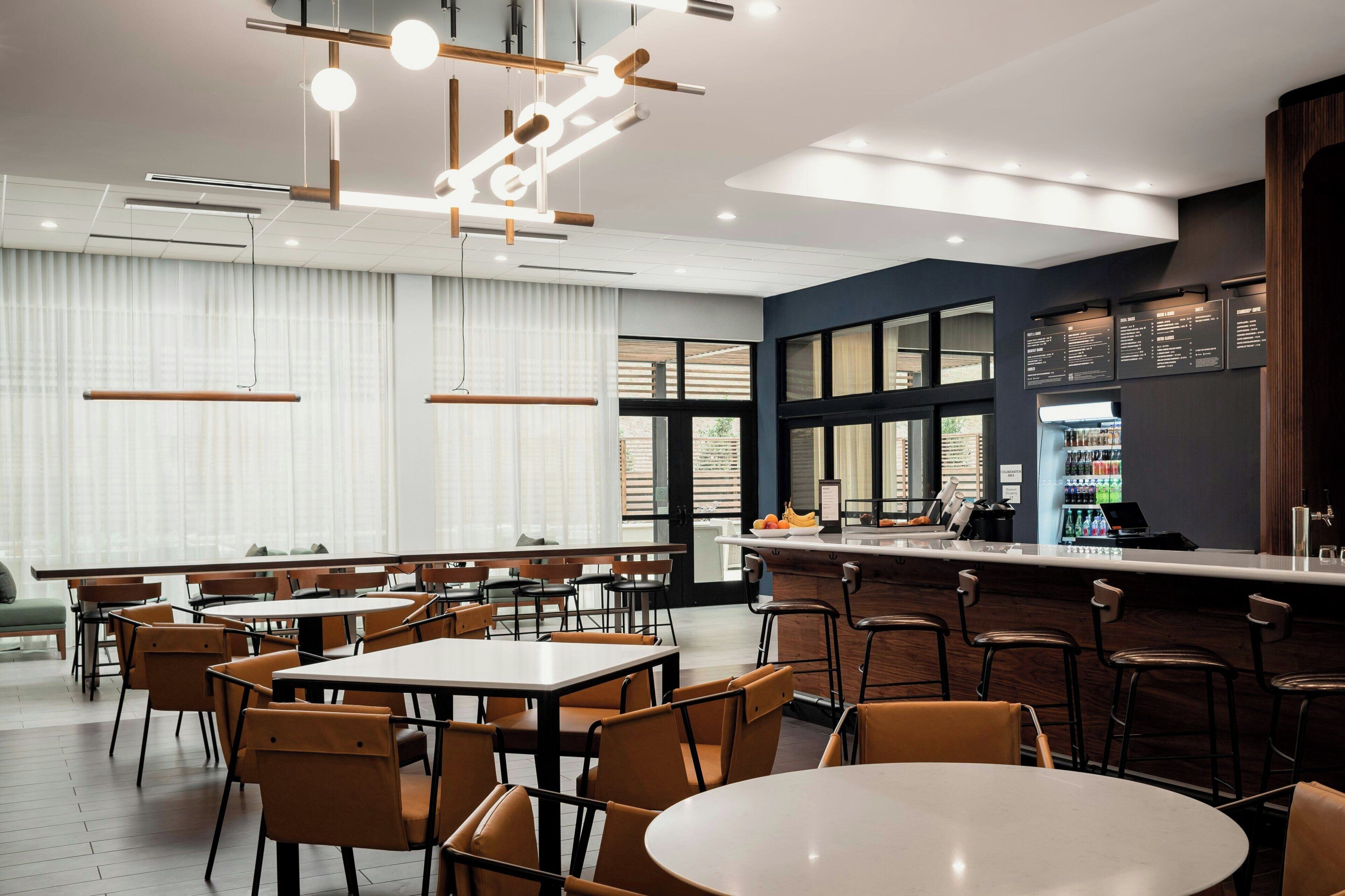 Uma sala de jantar moderna com várias mesas, cadeiras, um balcão de bar e um quadro de cardápio.