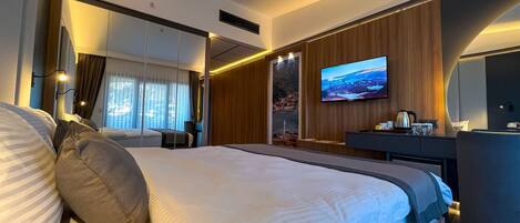 Quarto de hotel moderno com uma cama grande, uma TV de tela plana, uma escrivaninha com cadeira e uma janela ampla com cortinas.
