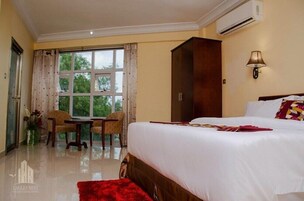 Quarto de hotel com uma cama grande, uma escrivaninha e uma cadeira perto da janela.