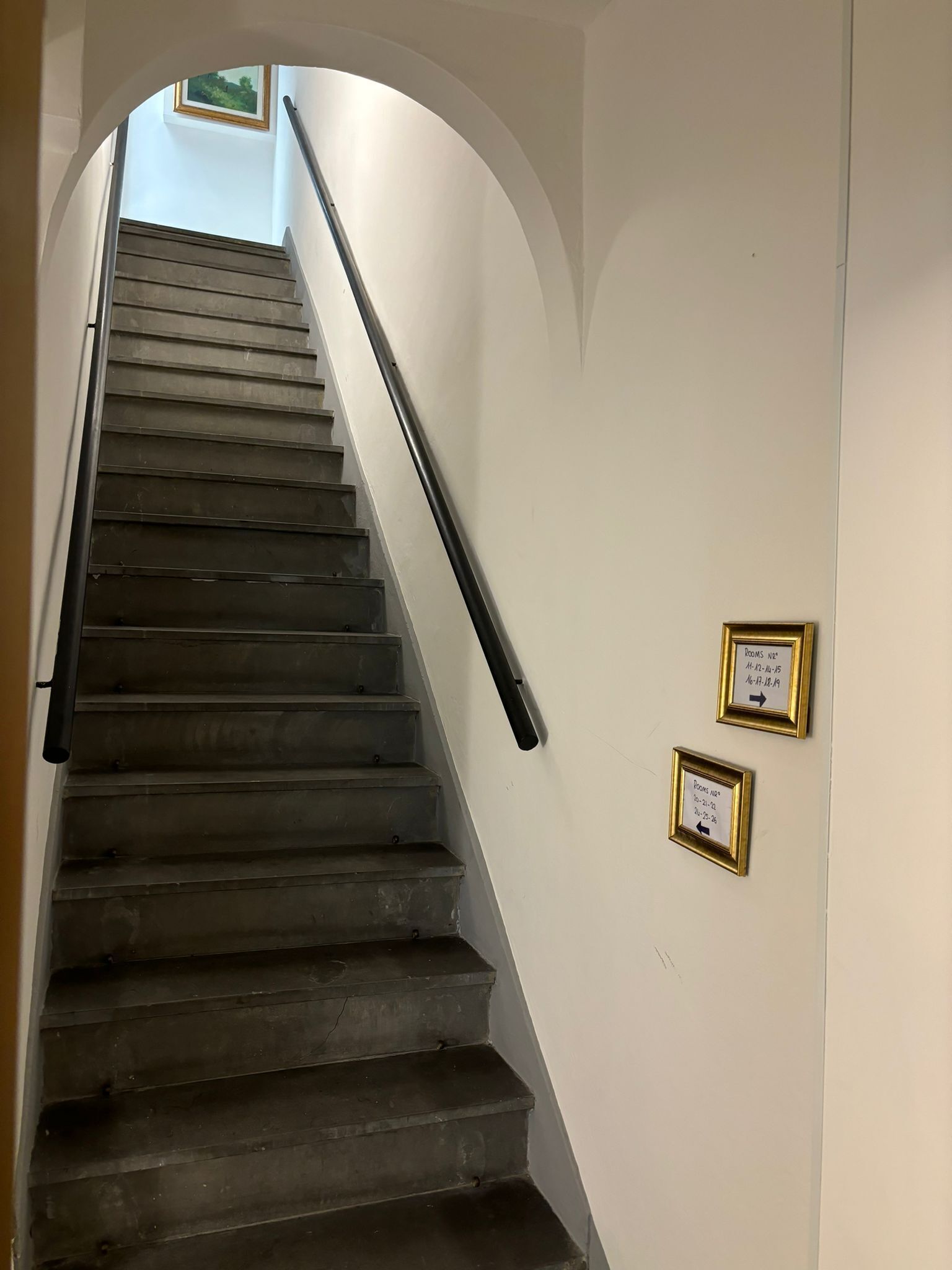 Uma escada com corrimão, levando a um patamar com uma moldura na parede.