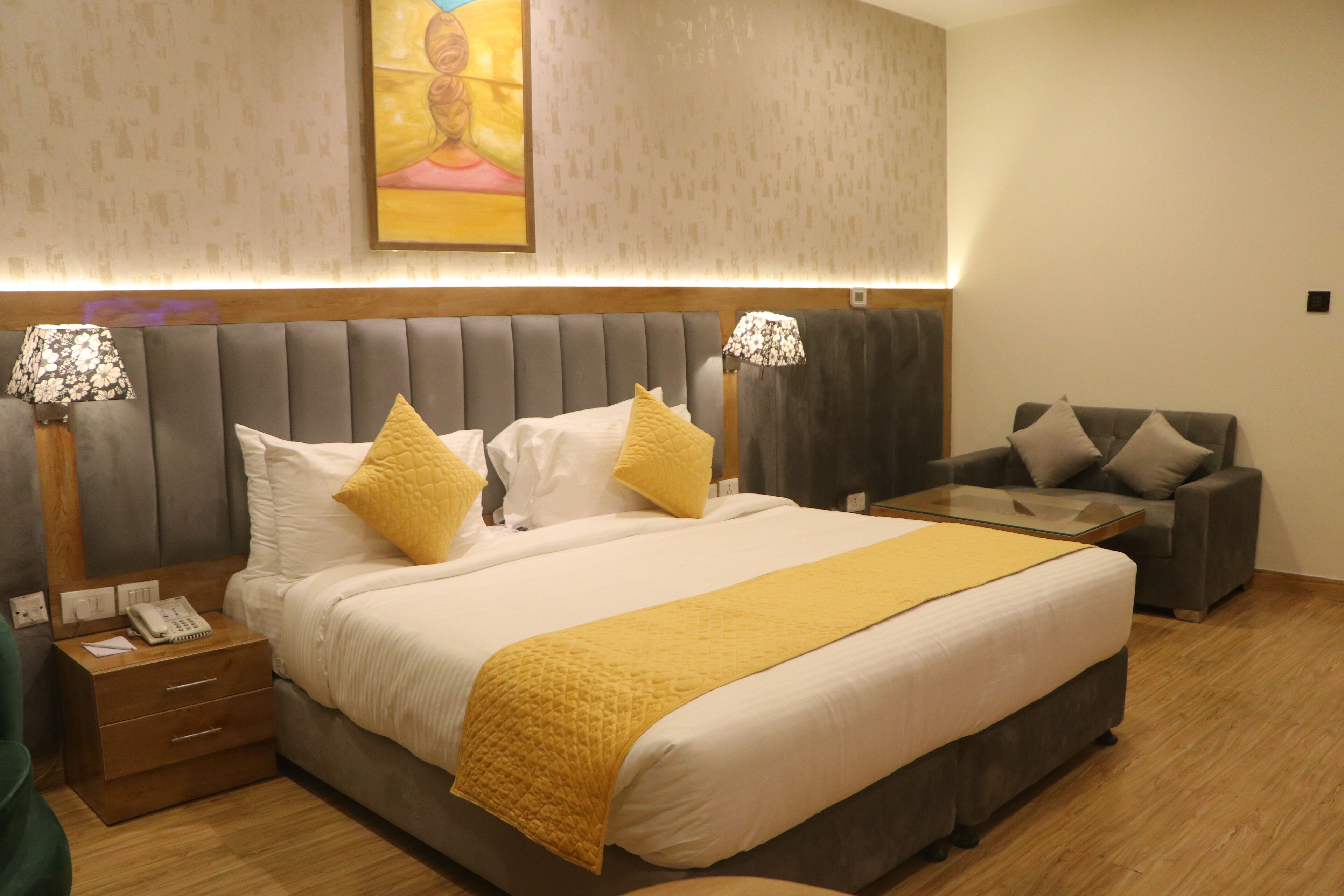 Quarto de hotel com uma cama grande, duas mesas de cabeceira, um sofá e um quadro na parede.