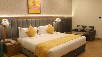 Quarto de hotel com uma cama grande, duas mesas de cabeceira, um sofá e um quadro na parede.