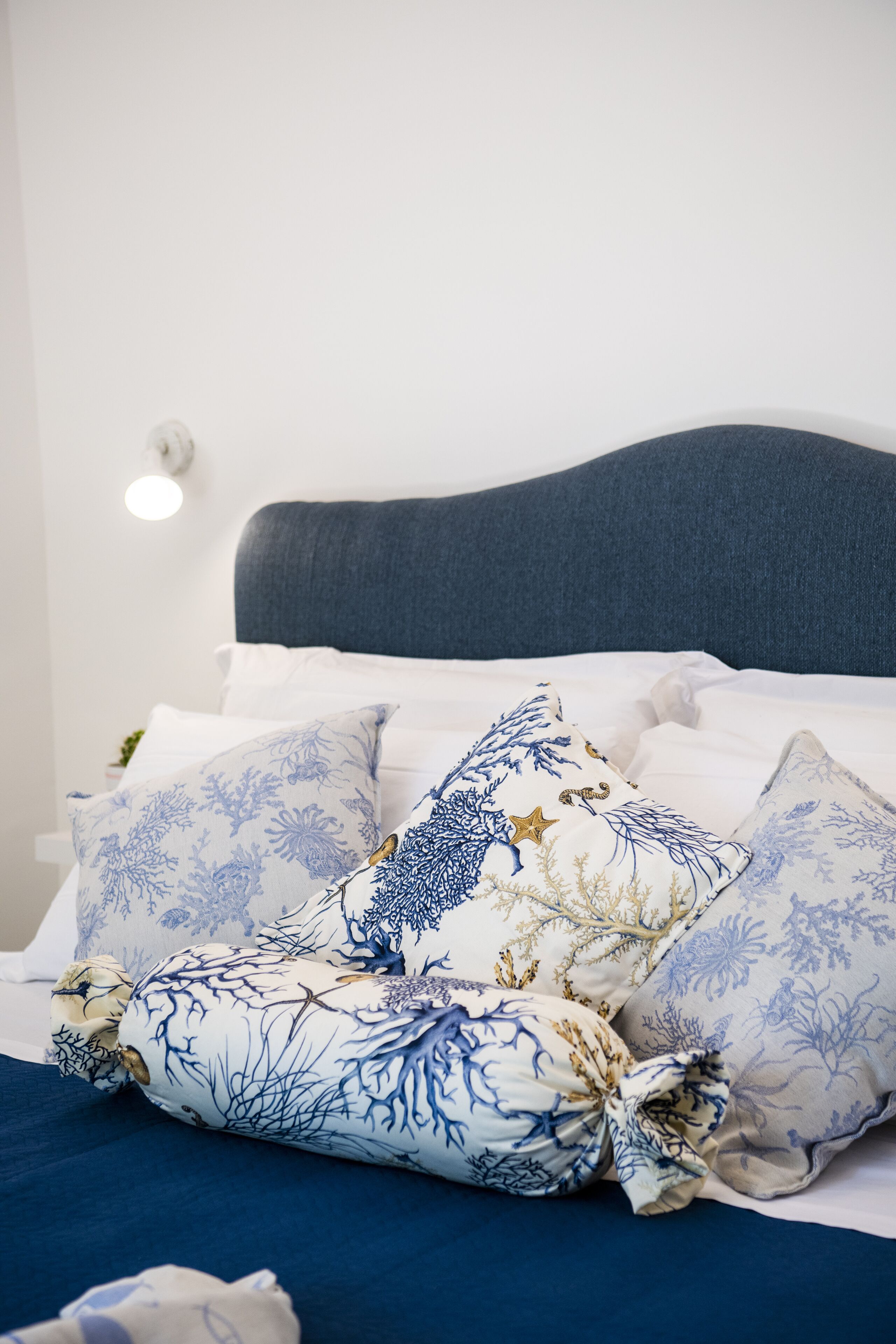 Cama bem arrumada com almofadas estampadas em azul e branco e uma cabeceira escura.