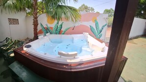 Uma banheira de hidromassagem com estrutura de madeira, cercada por um espaço de terraço com cadeiras e um mural na parede.
