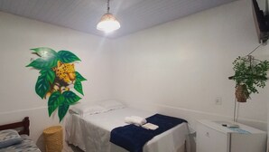 Quarto pequeno e limpo, com cama, mesa de cabeceira, planta pendente e um mural de leopardo na parede.