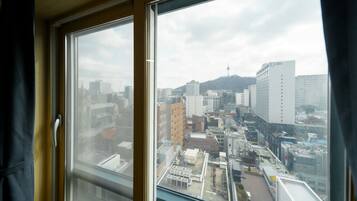 Vista da janela sobre uma paisagem urbana com vários edifícios e uma torre imponente ao longe.