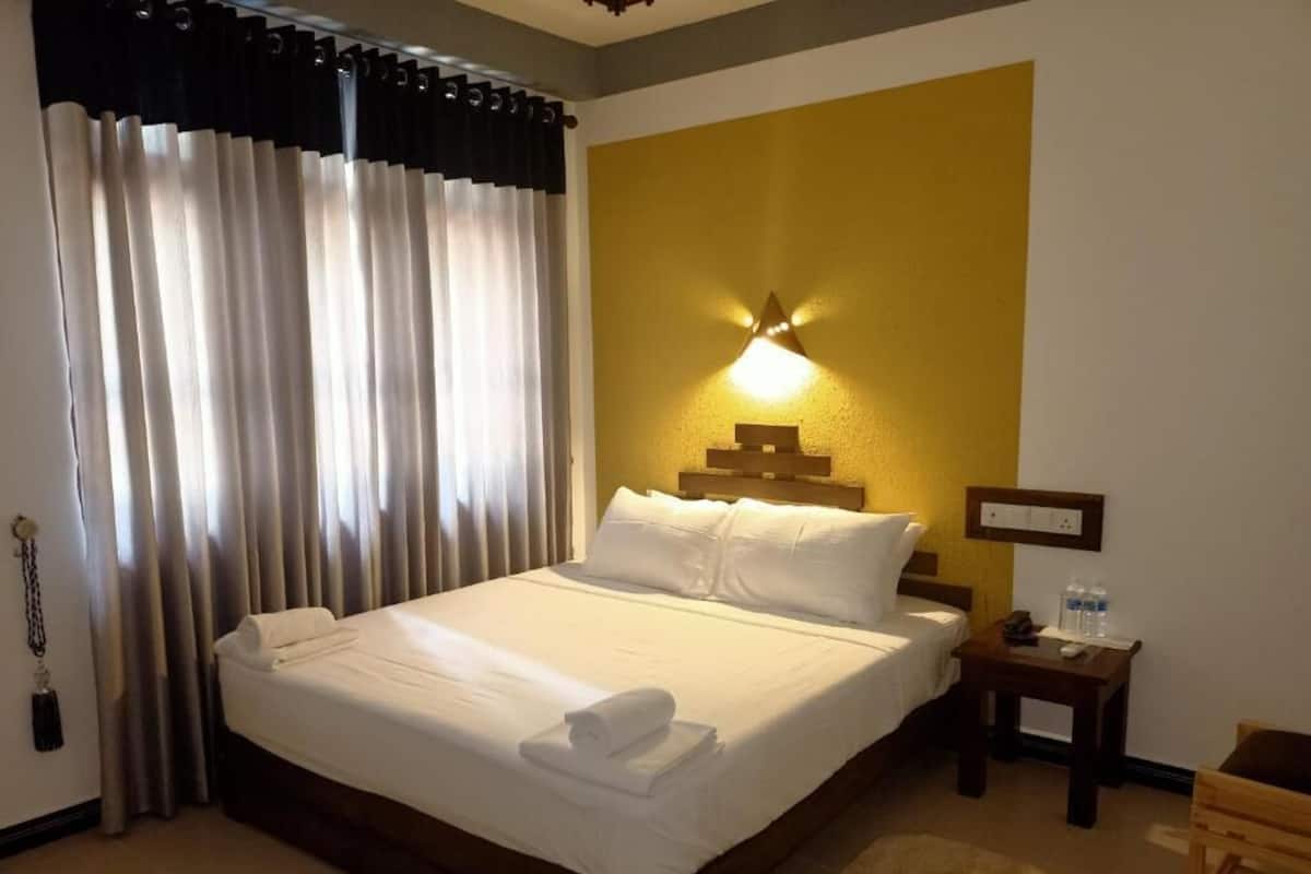 Quarto de hotel com uma cama grande, uma mesa de cabeceira, uma luminária e uma cadeira de madeira.