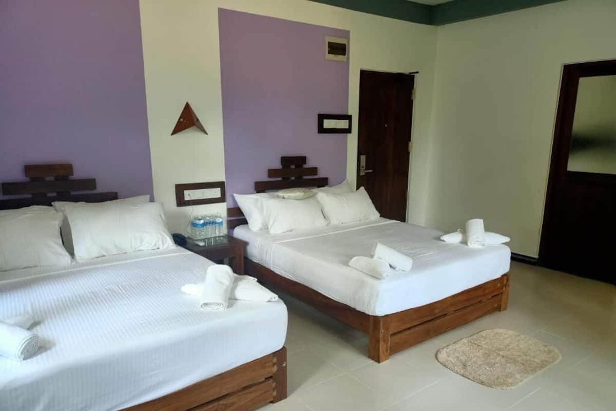 Quarto de hotel com duas camas, cada uma com lençóis e toalhas brancas, uma cabeceira de madeira e um tapete pequeno no chão.