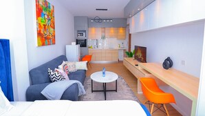 Um espaço compacto com sofá, uma mesinha redonda, cozinha equipada com micro-ondas e uma mesa de jantar com cadeiras laranja.