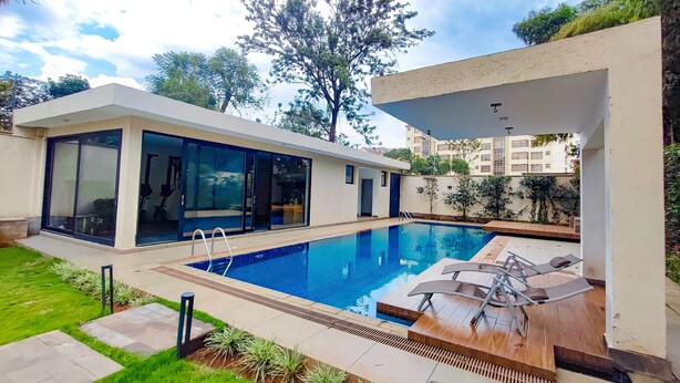 Uma área de piscina moderna ao ar livre, com uma piscina azul cristalina, um espaço coberto para relaxar e uma estrutura envidraçada.
