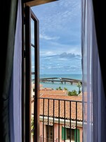 Vista da janela com uma paisagem costeira, incluindo uma ponte e edifícios com telhados vermelhos.