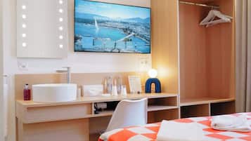 Quarto de hotel com cama, escrivaninha, espelho, televisão e guarda-roupa.