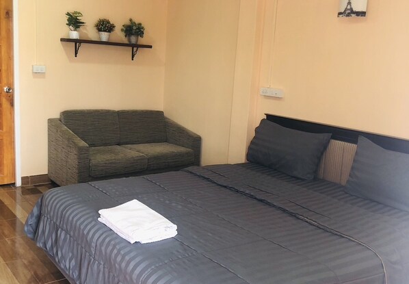 Quarto com cama, sofá cinzento e prateleira fixada na parede com plantas.
