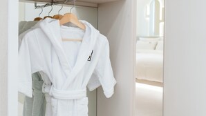 Um robe branco pendurado em um cabide de madeira dentro de um armário, com um espelho refletindo uma cama ao fundo.