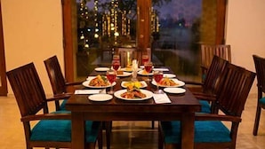 Mesa de jantar posta para seis, com cadeiras, pratos de comida e copos.