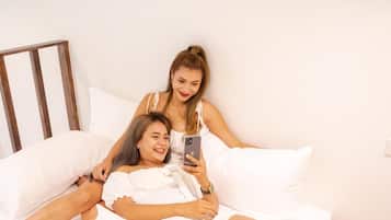 Duas pessoas em uma cama com roupa de cama branca e cabeceira de madeira.