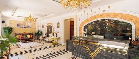 Um hall imponente com uma receção de mármore, lustres ornamentados e um quadro grande na parede.