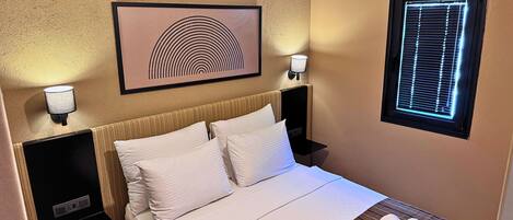 Quarto de hotel com cama, mesas de cabeceira, luminária na parede, ar condicionado e janela com persianas.