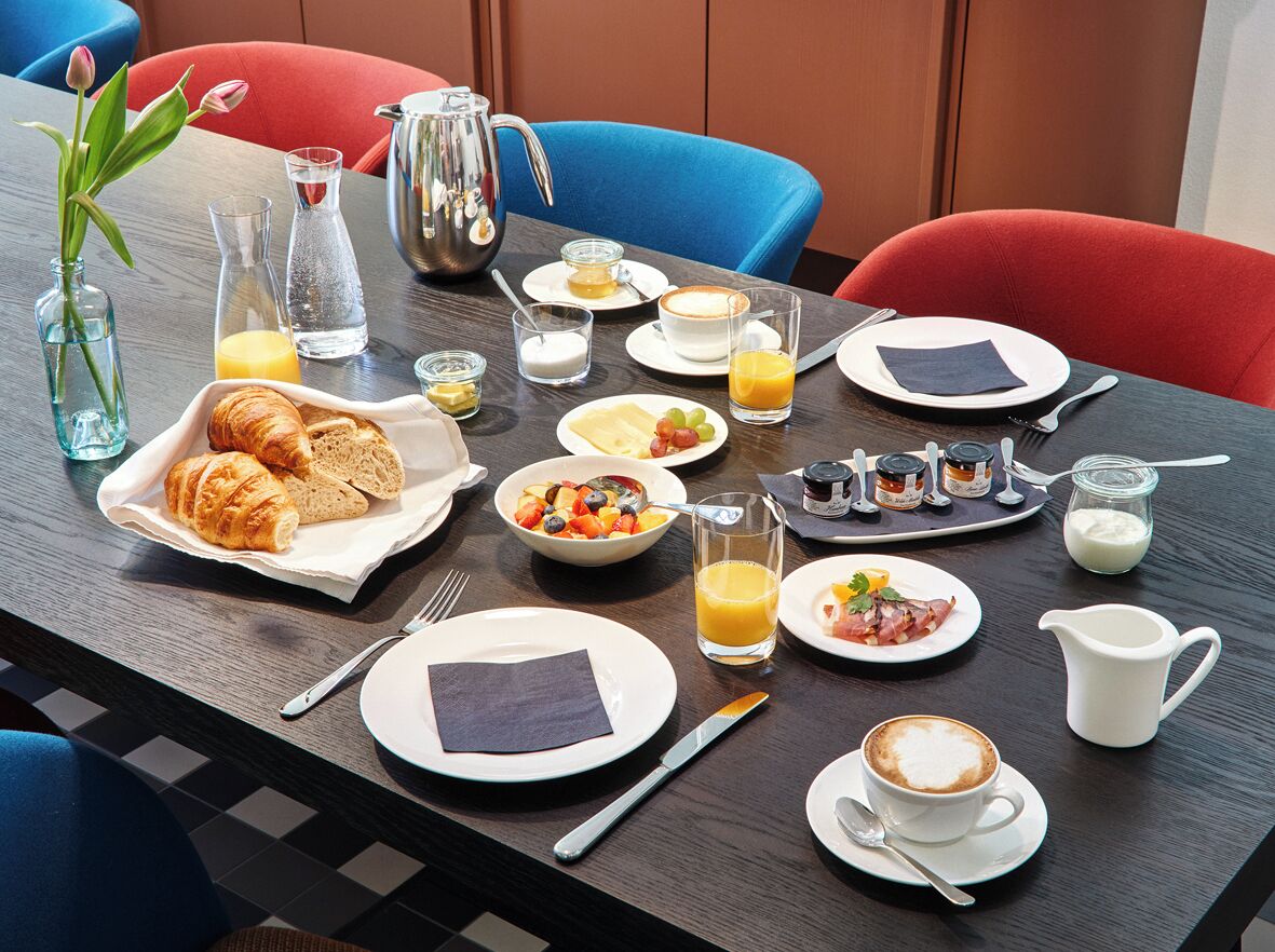 Mesa de café da manhã posta com croissants, frutas, café e suco.