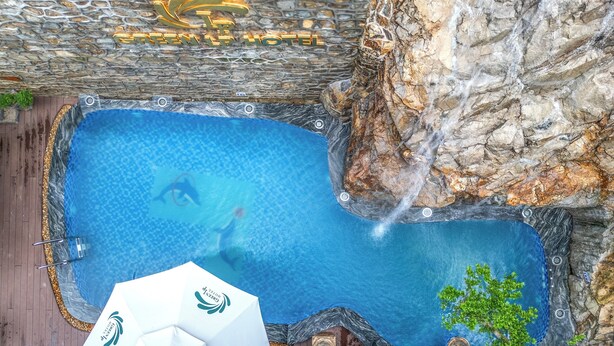 Piscina com cascata, rodeada por um muro de pedra e um deck de madeira.