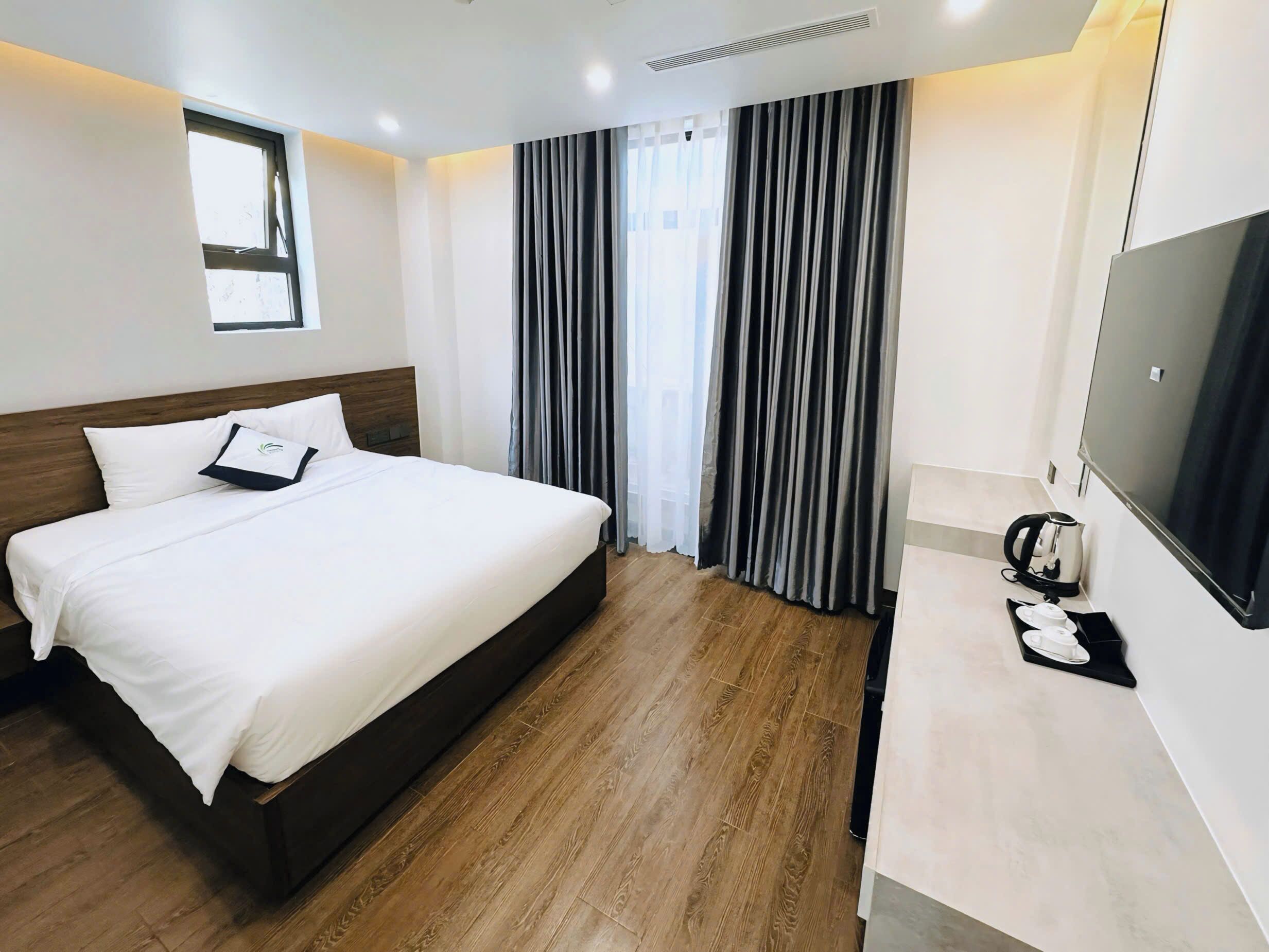 Quarto de hotel com uma cama grande, televisão de tela plana, cafeteira e janela com cortinas.